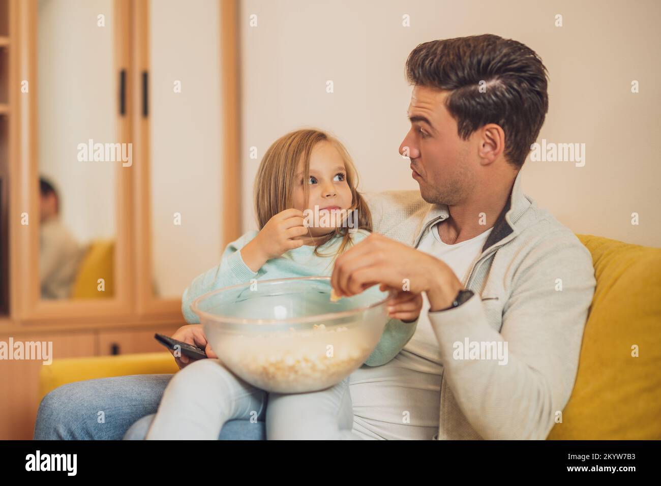 Surprised father and daughter watching tv and eating pop corns together ...