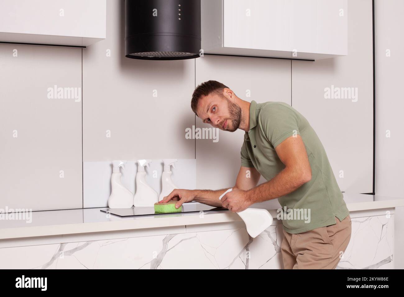 Man cleaning the cooker in the kitchen holding bottle with blank label ...