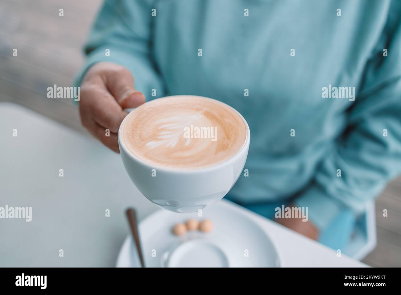 Woman hands holding a white cup of latte coffee standing on the table ...