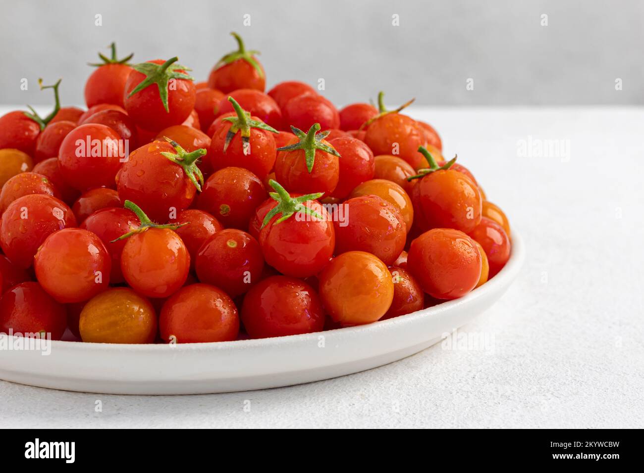 Red cherry tomatoes in a white dish on a light Stock Photo - Alamy