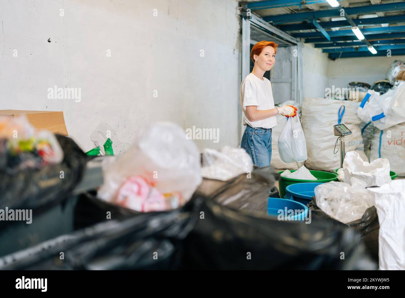 Portrait of positive female volunteer worker in latex gloves sorting ...