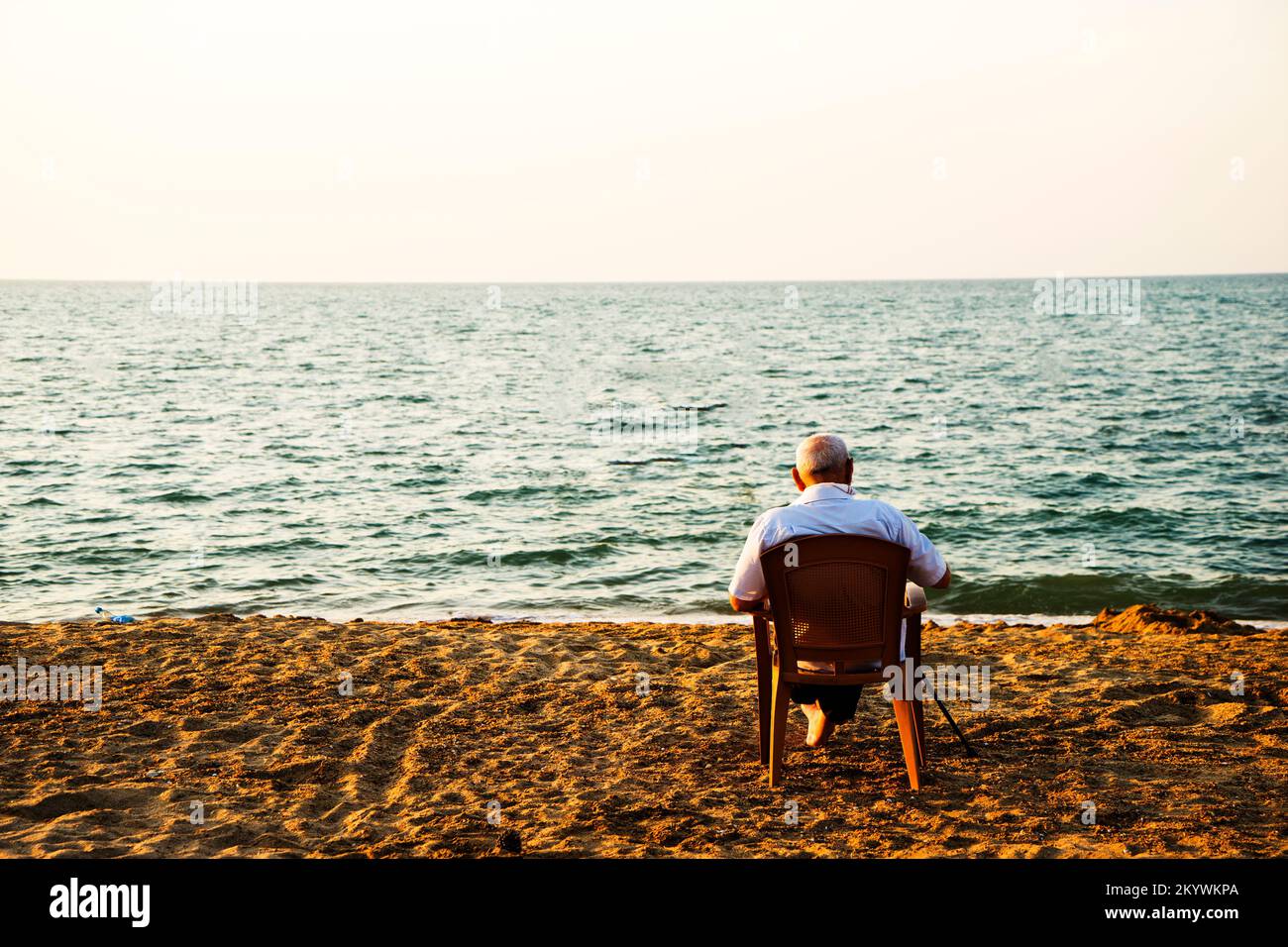 old man sitting on a chair on the beach and looking at the sea Stock ...