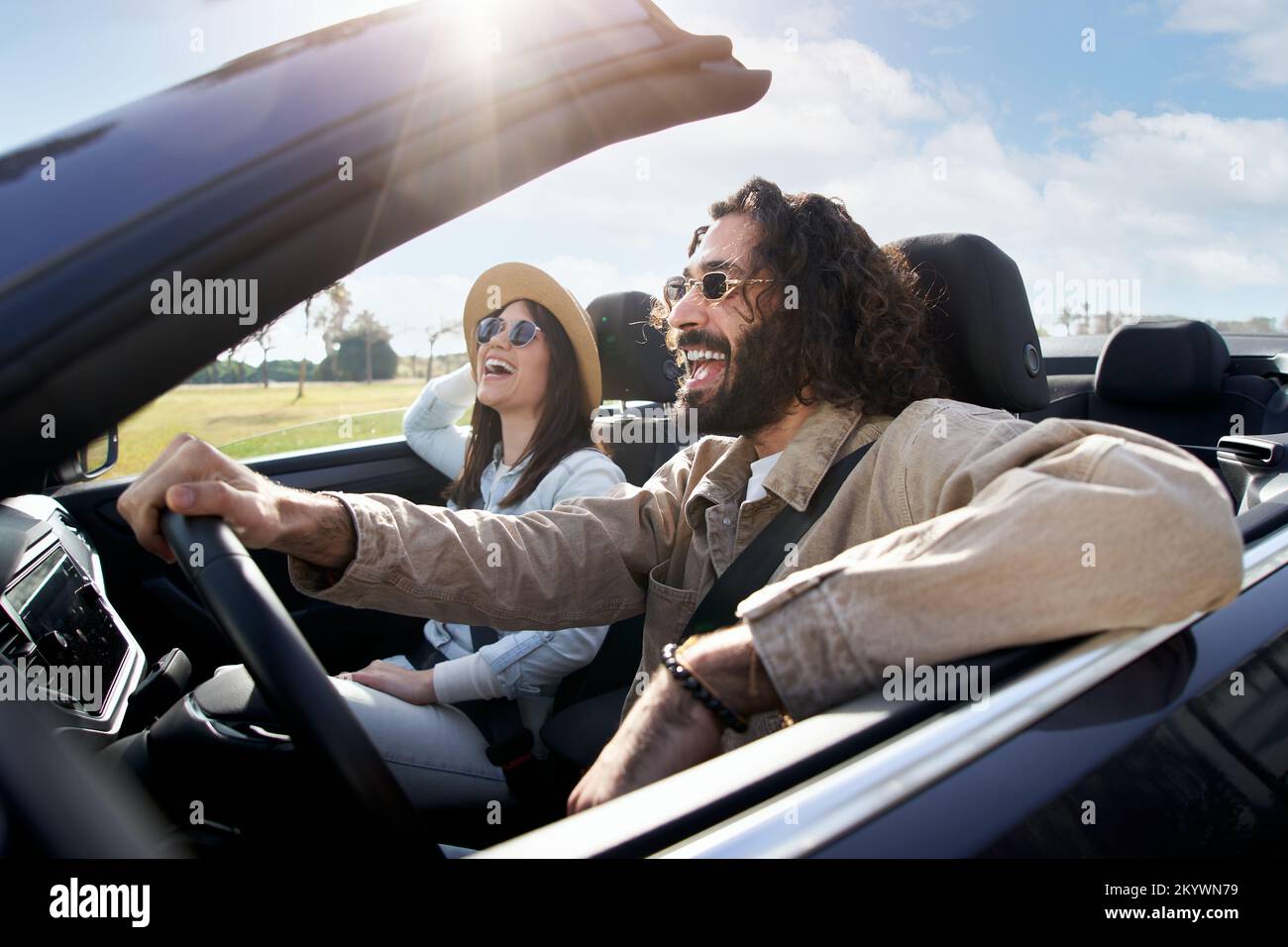 A young cheerful Caucasian couple driving in a convertible car enjoying ...