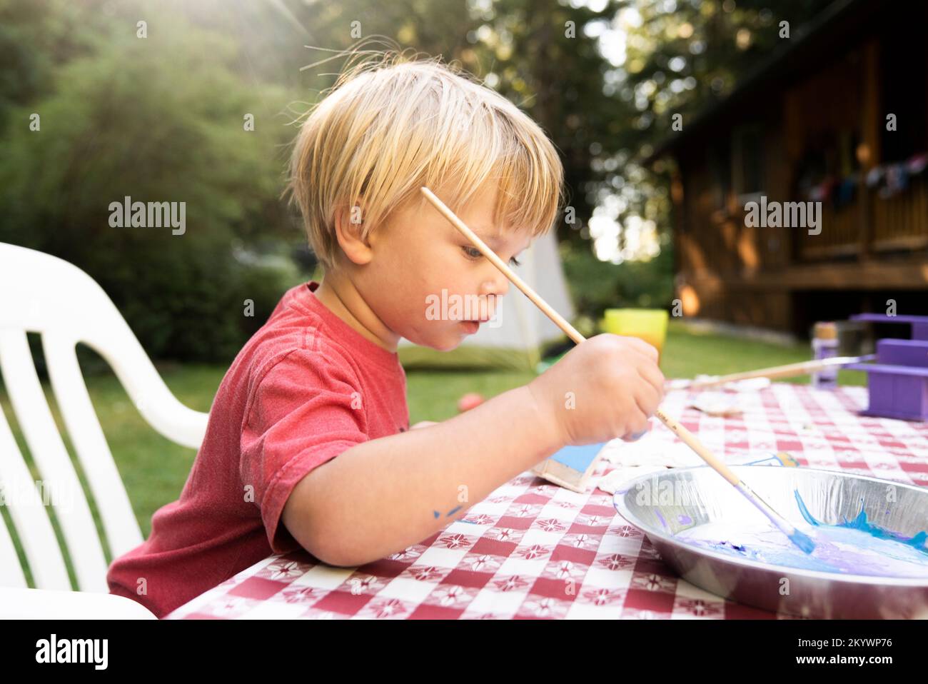 A young boy paints at an outdoor table near a cabin Stock Photo - Alamy