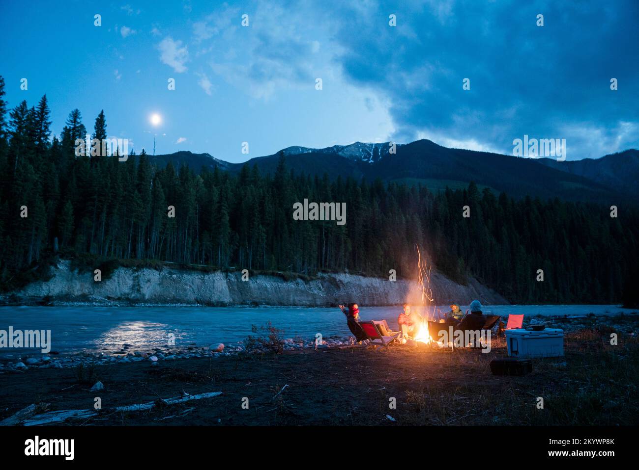 A group of adults sit around campfire beside wilderness river Stock ...