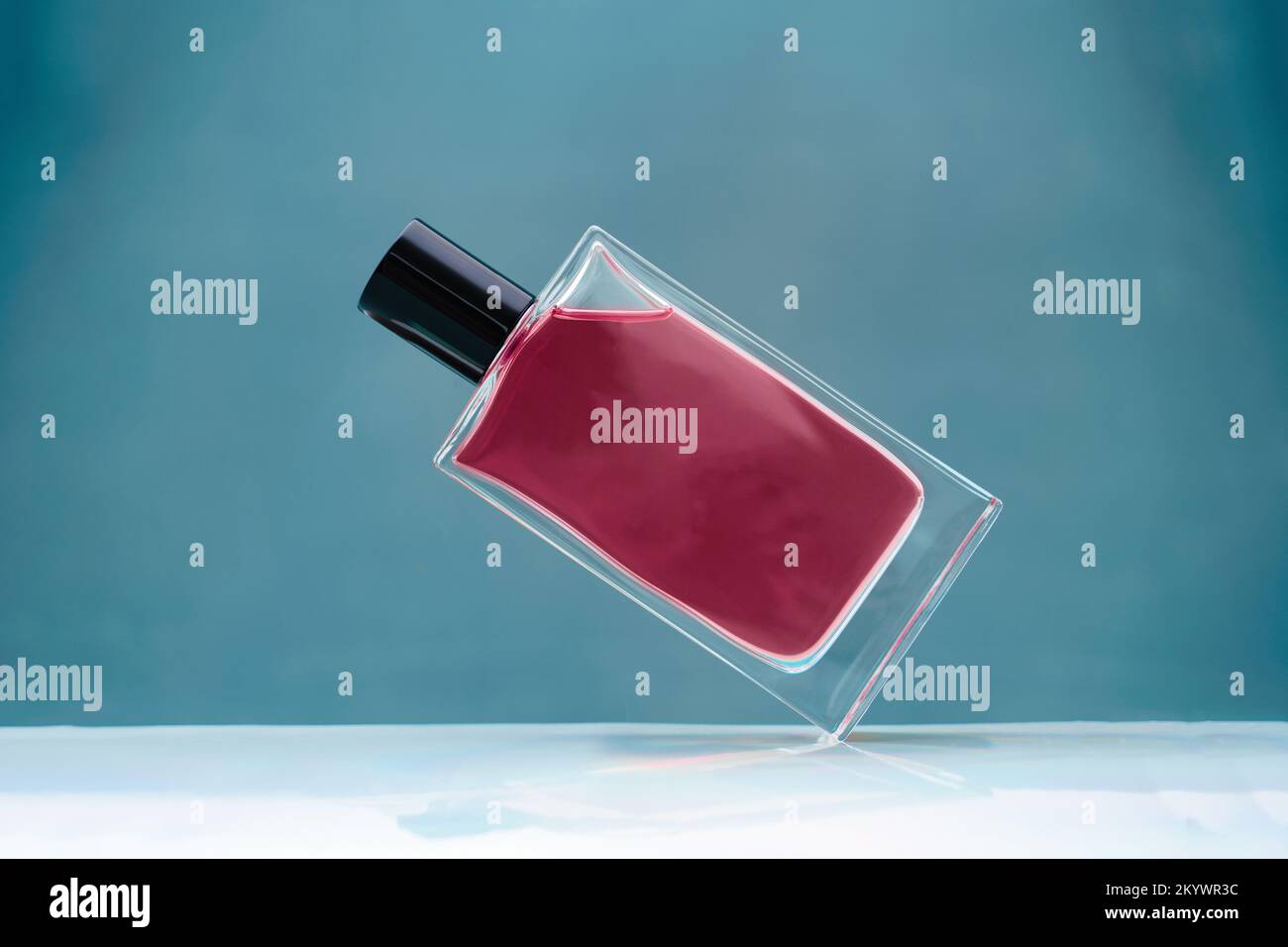 Suspended glass magenta perfume bottle with black cap on blue ...