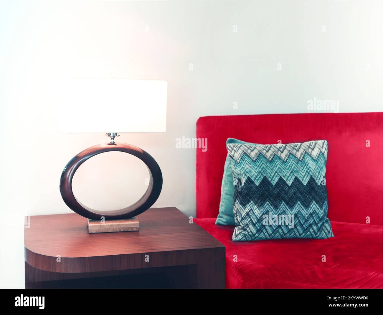 Elegant wooden table with lamp placed near cozy couch with cushions in ...