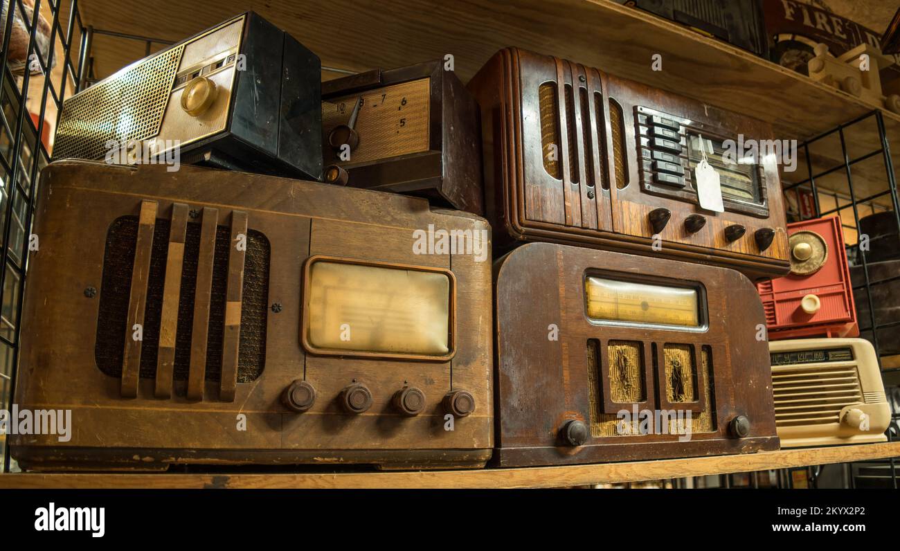 A variety of vintage table top radios grouped together on a shelf ...