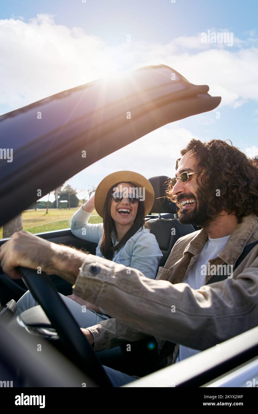 A young cheerful Caucasian couple driving in a convertible car enjoying ...