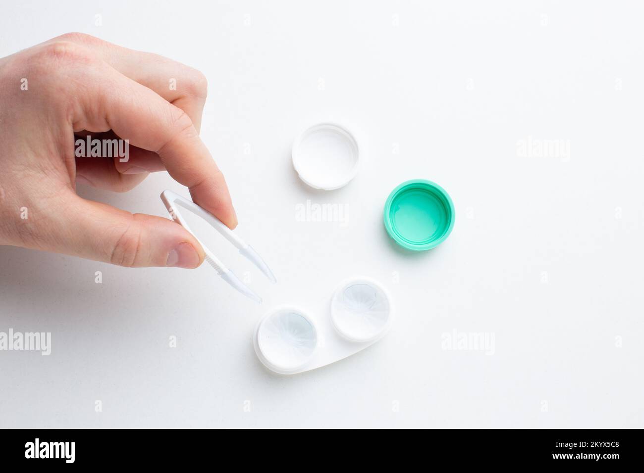 Hands picking up a contact lens with tweezers and maintenance material ...