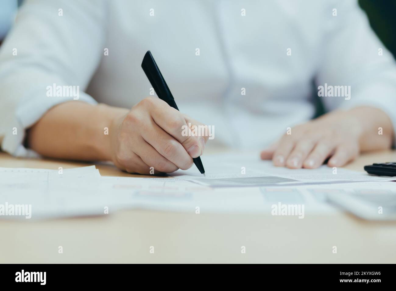 Close-up photo. Male hands at the table writing with a pen on paper ...