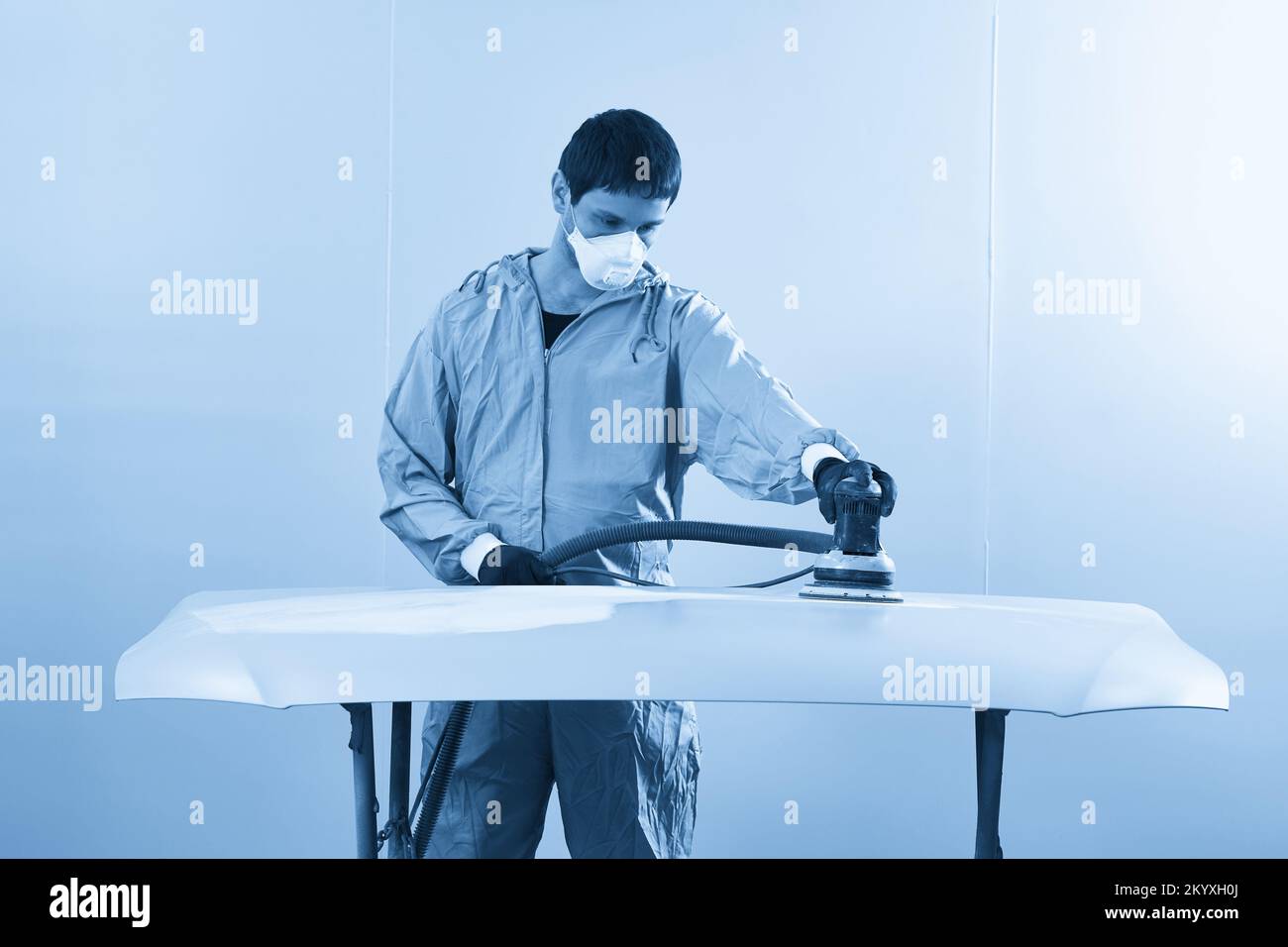 Auto mechanic wearing face mask buffing and polishing car hood in auto ...