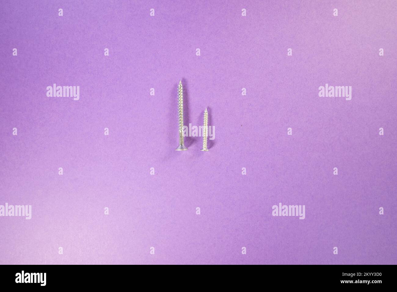 one small and one large new unused silver screws isolated on a purple ...