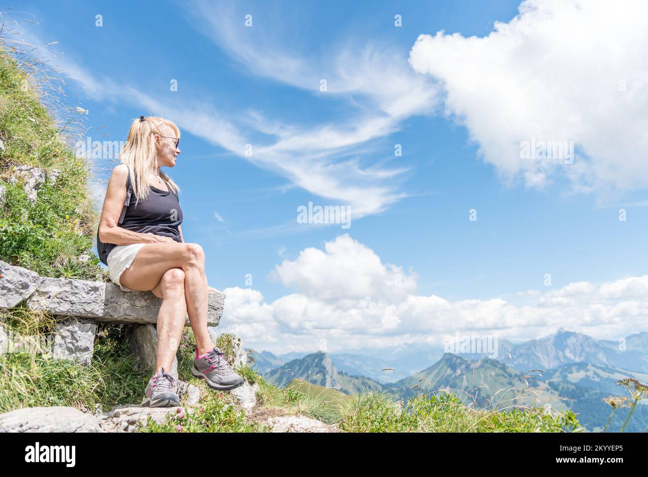 Mature blonde woman with sunglasses sitting cross-legged looking at the ...