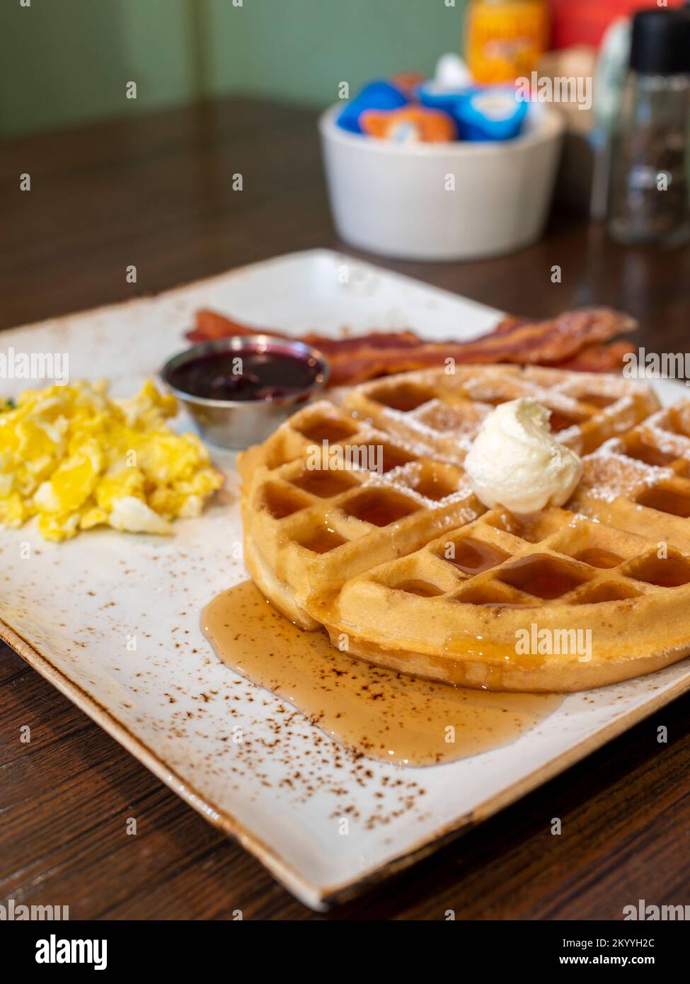 American breakfast with a Belgian waffle, scrambled eggs and bacon on a ...