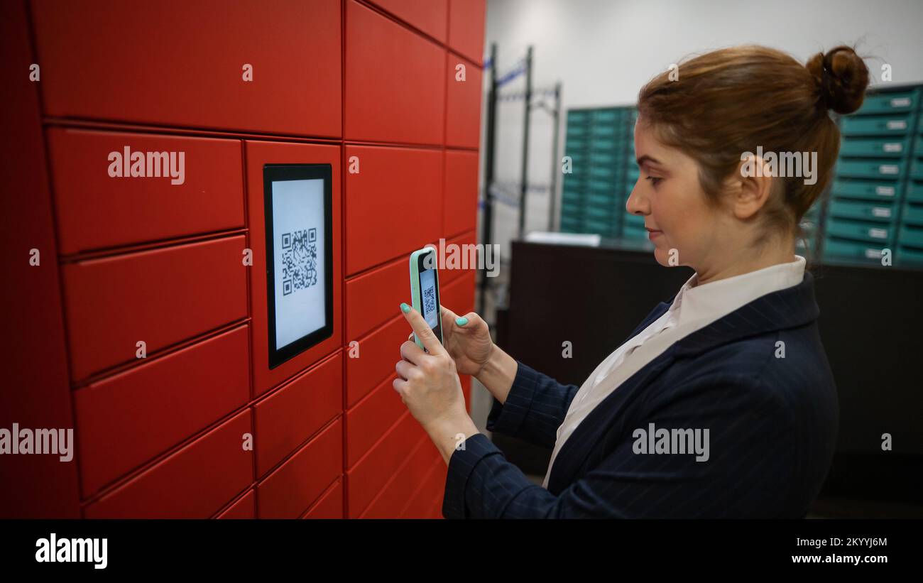A woman scans a red code to pick up a parcel at a parcel machine ...