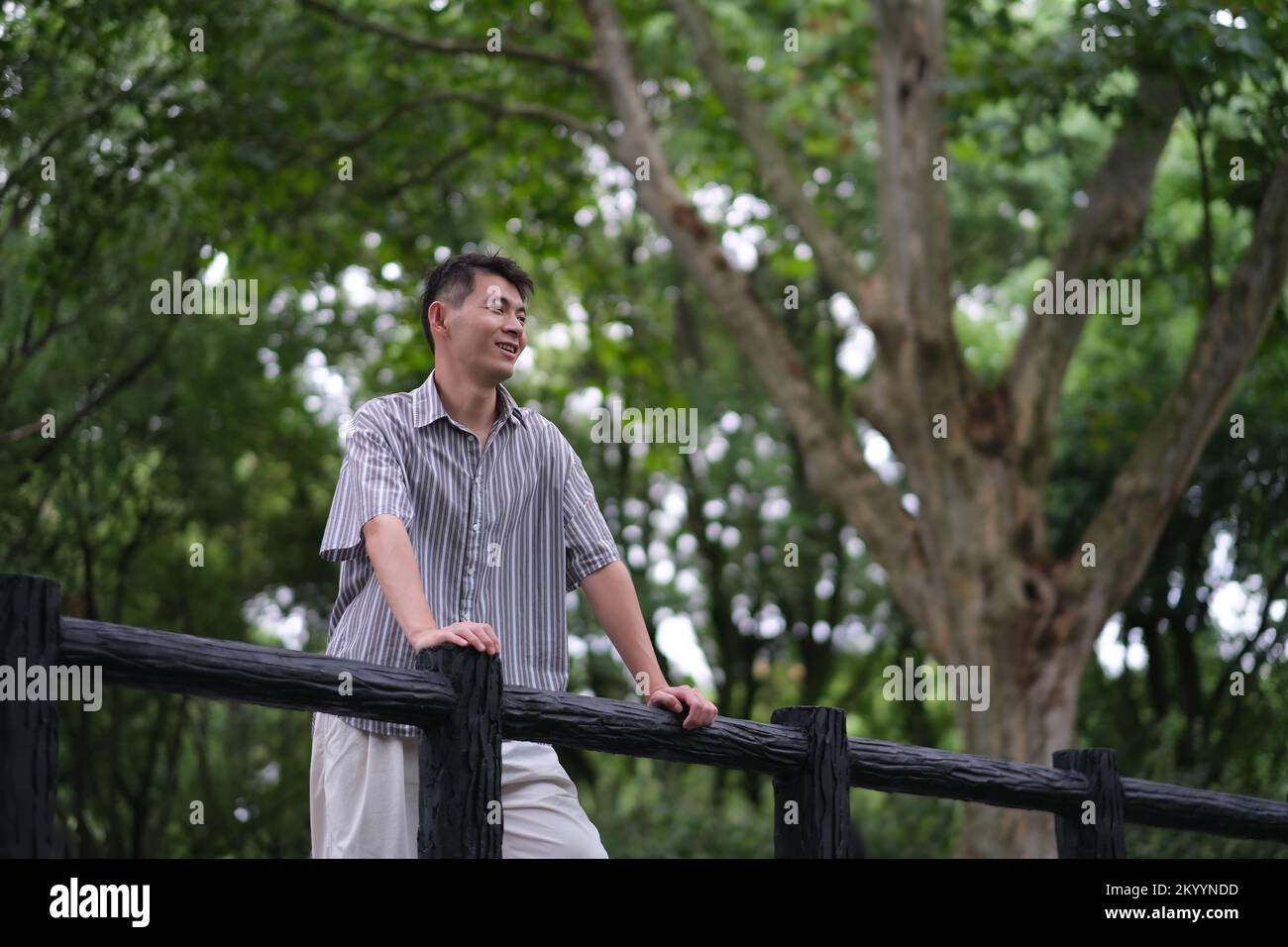 smiling Asian young man at outdoor green forest park at summer, looking ...