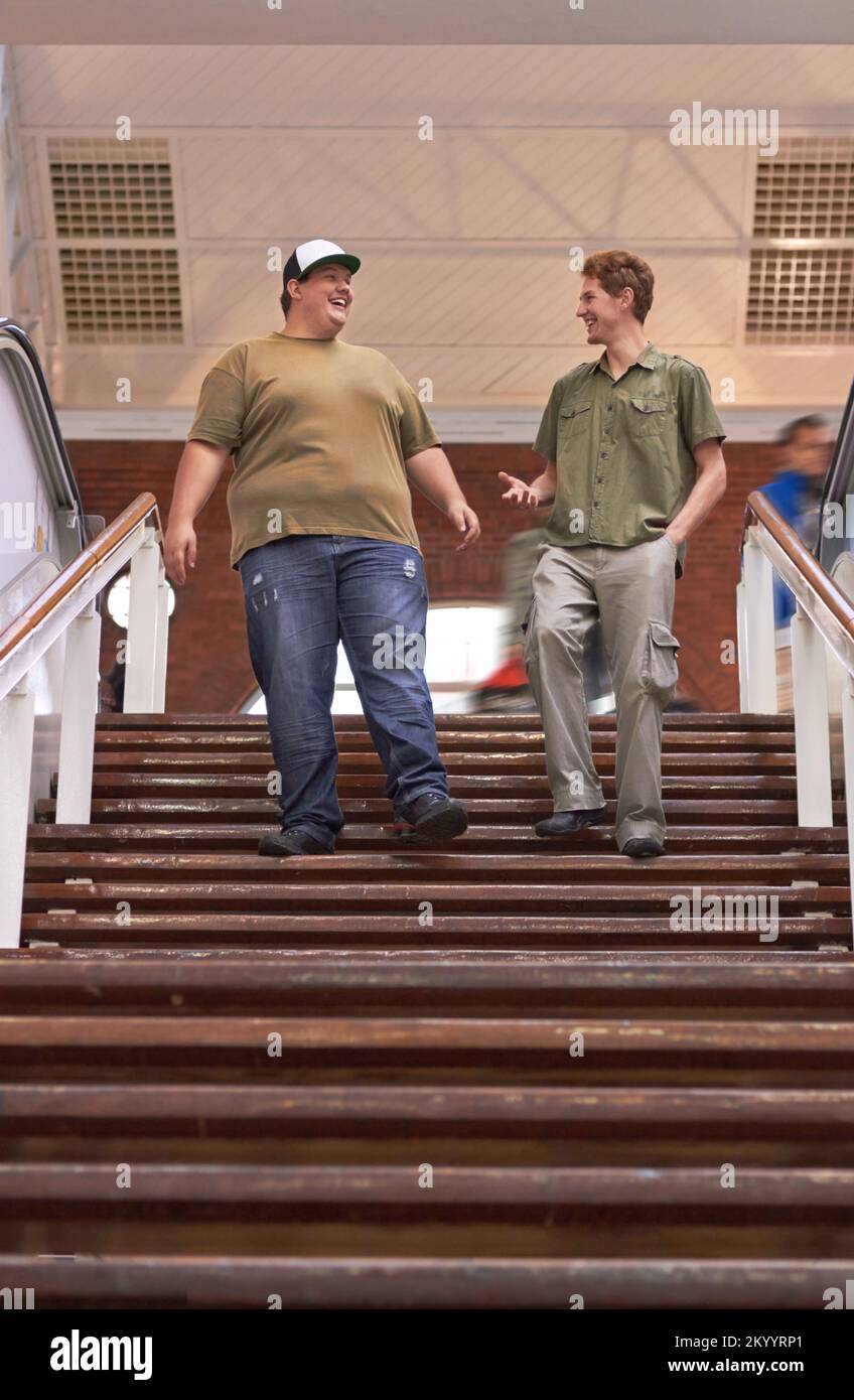 Stepping out. Two young men walking down a flight of stair together ...