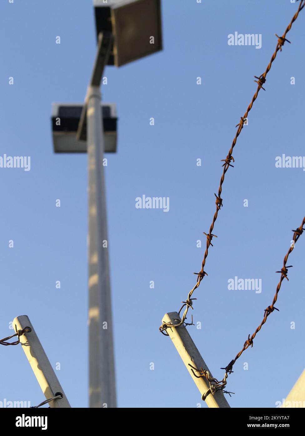Barbed wire security fence from low point of view against blue sky ...