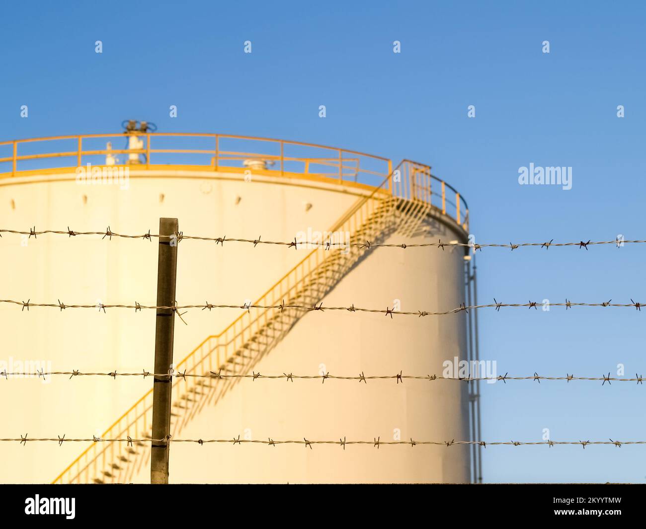 Barbed wire security fence around large circular fuel storage tanks ...