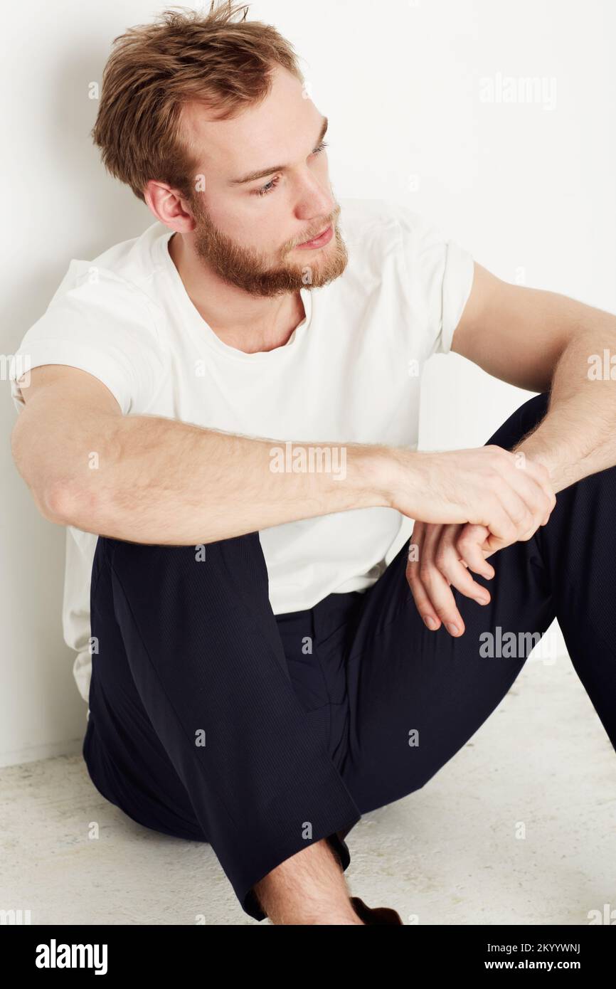 Thinking things over. A young man sitting on the floor against a wall Stock Photo - Alamy