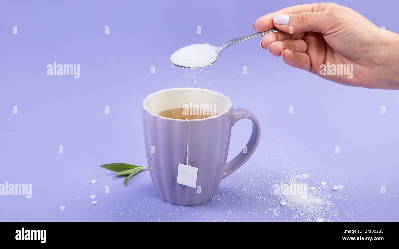 Hand with spoon of sugar. Cup of tea. Artificial sugar on a violet ...