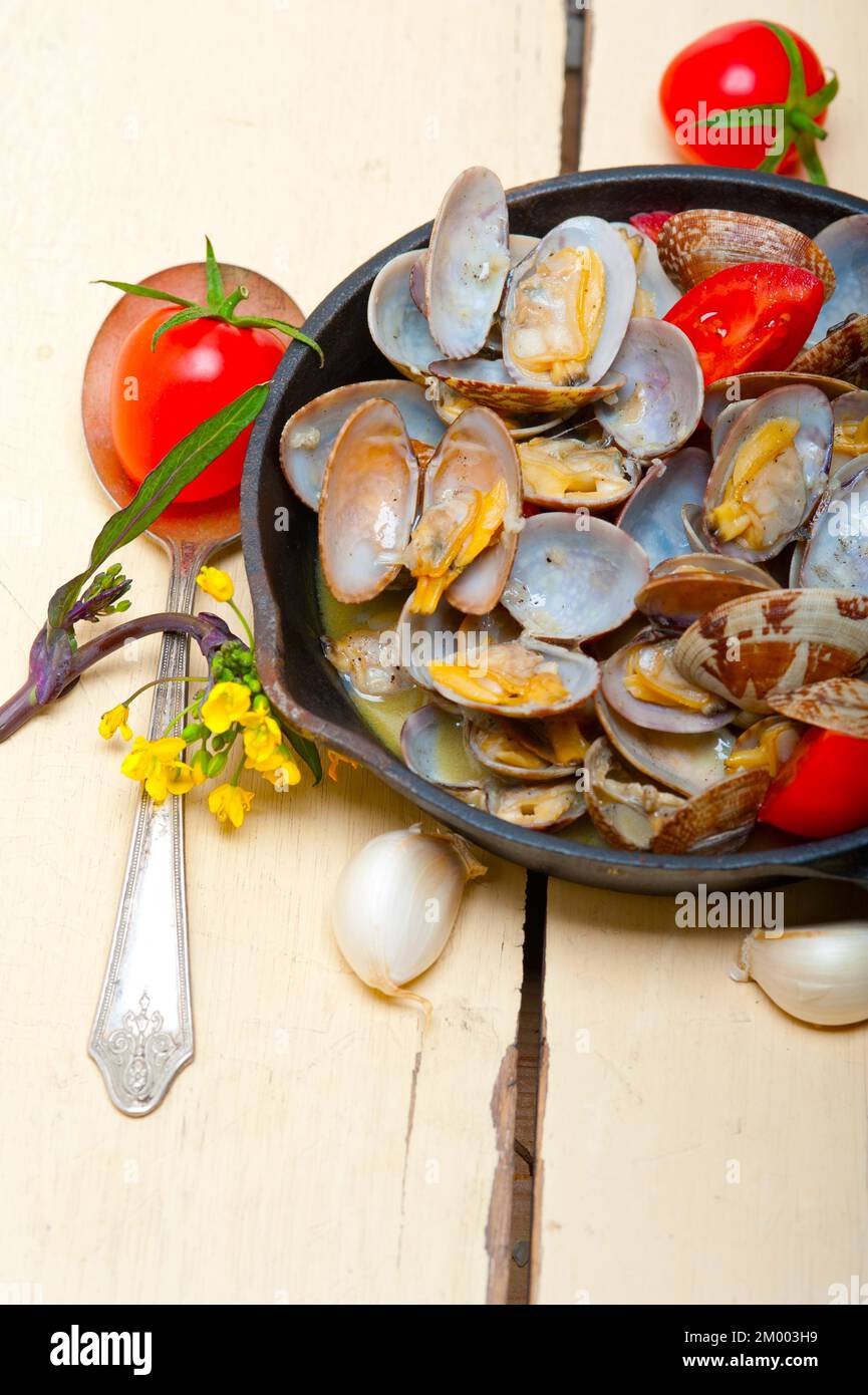 Fresh clams stewed on an iron skillet over wite rustic wood table Stock ...