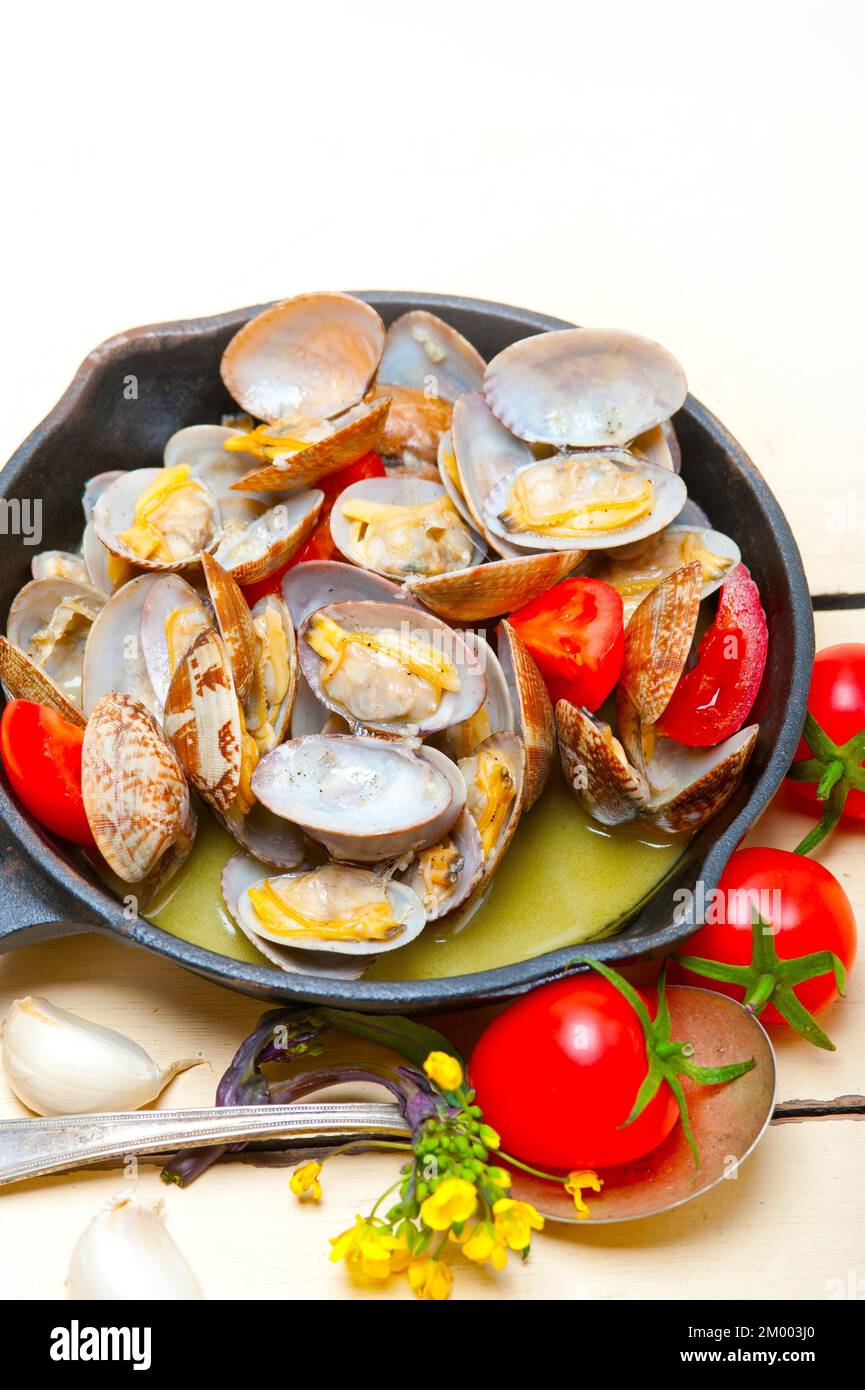Fresh clams stewed on an iron skillet over wite rustic wood table Stock ...