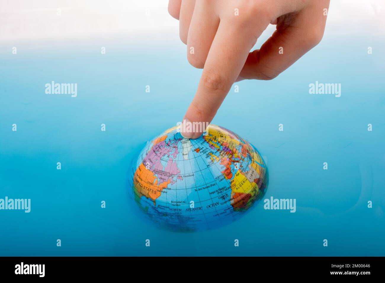 Little globe with finger on top floating in blue water Stock Photo - Alamy