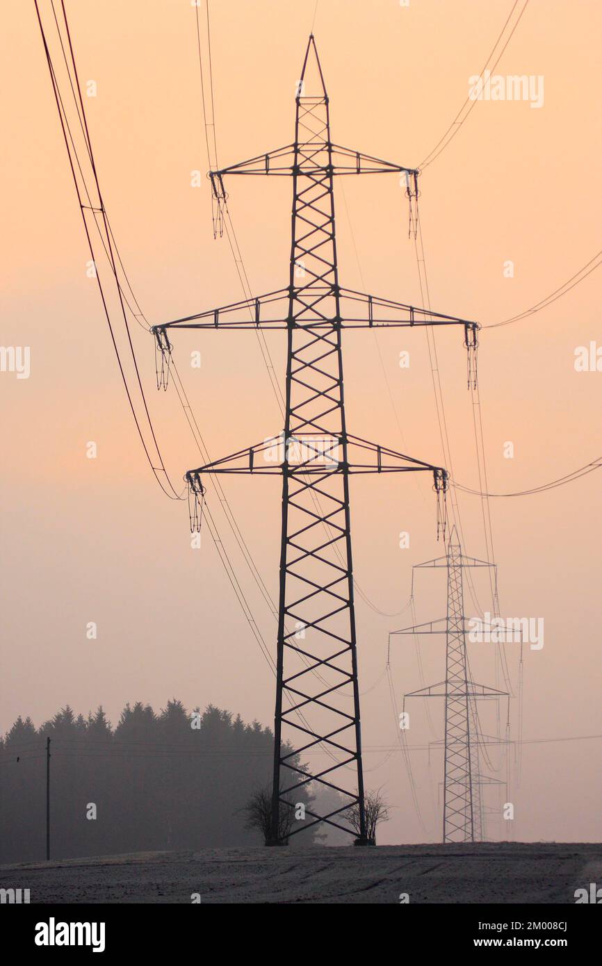 Silhouettes of high-voltage power line pylons are shrouded in fog in ...