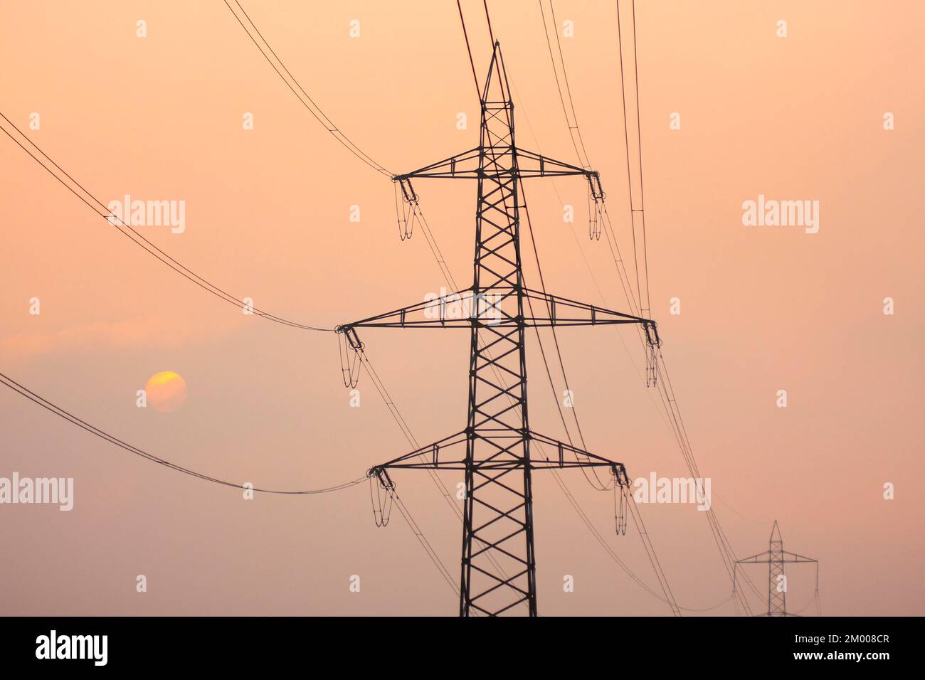 Setting sun behind silhouettes of high-voltage power line pylons ...