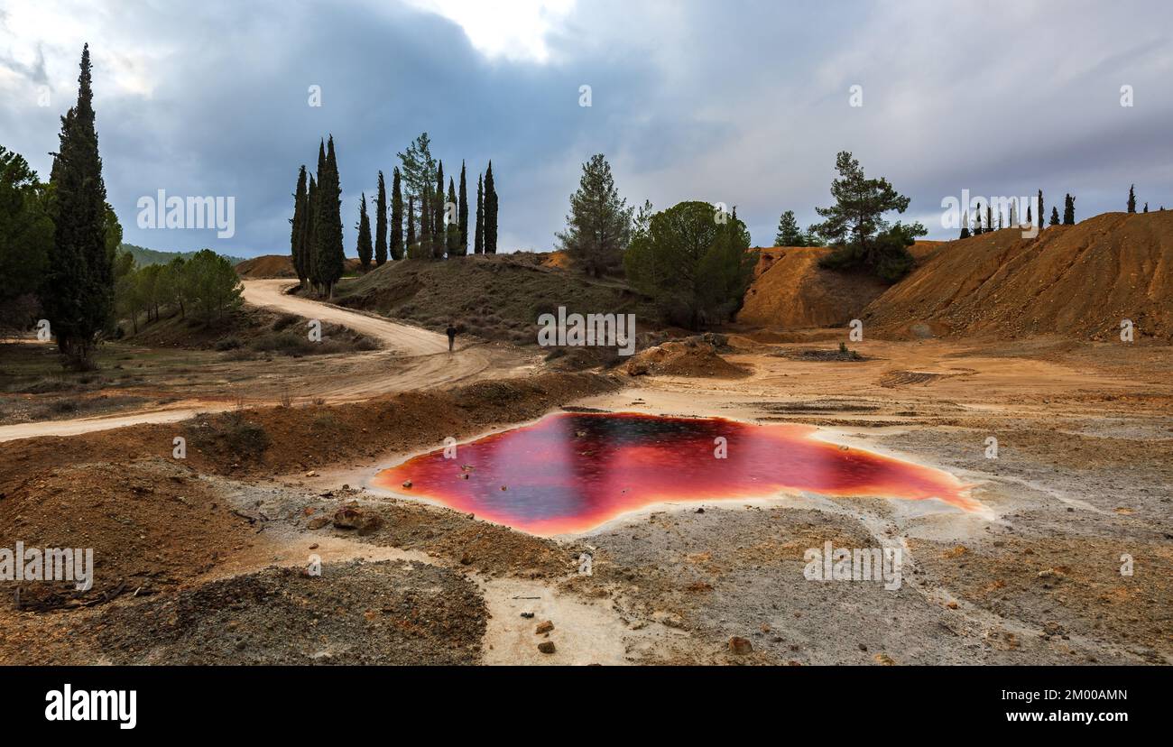 Unrecognizable man walking near a Lake with red polluted toxic water ...