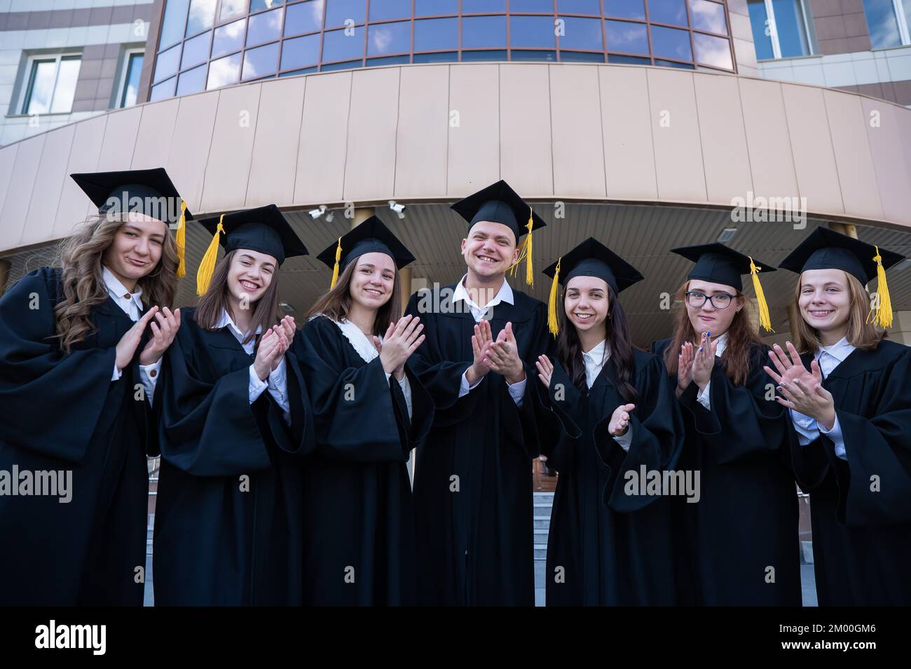 Seven graduates in robes stand in a row and clap outdoors Stock Photo ...
