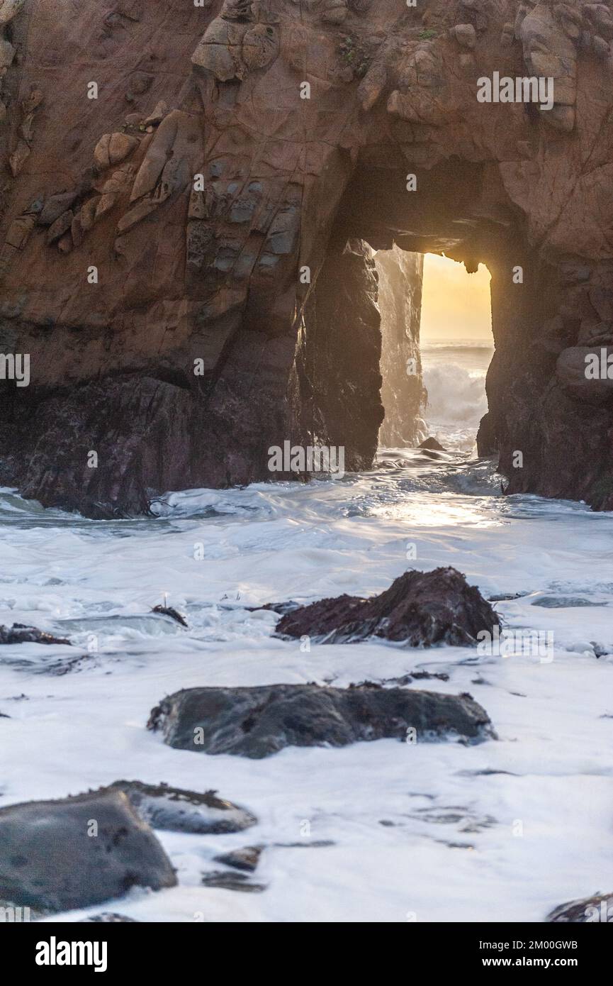 Stormy ocean water flowing through keyhole arch leaiving foam crests on ...