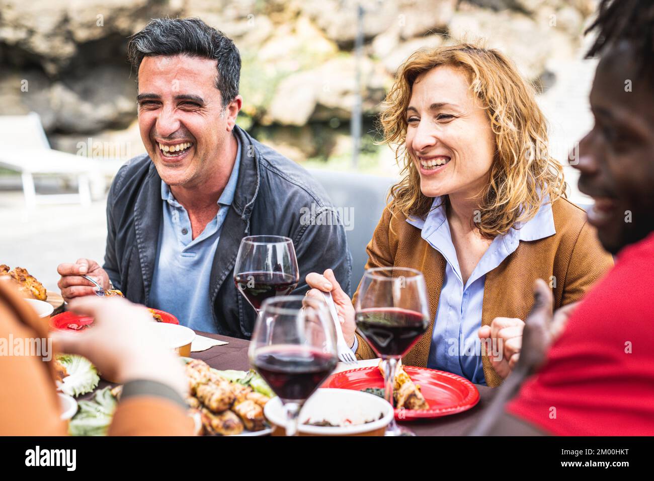 Adult people eating at barbeque and having fun drinking red wine ...