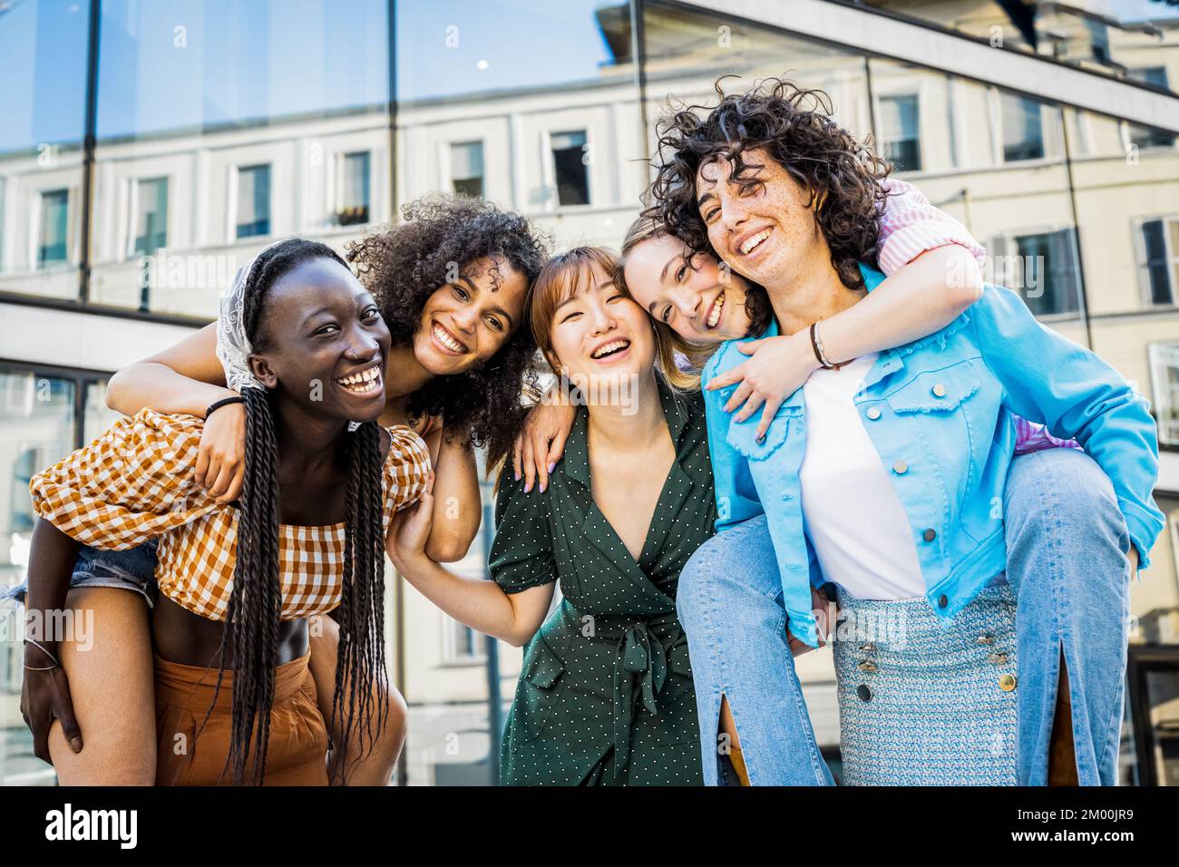 Portrait five friends women outdoor having fun hugging and riding ...