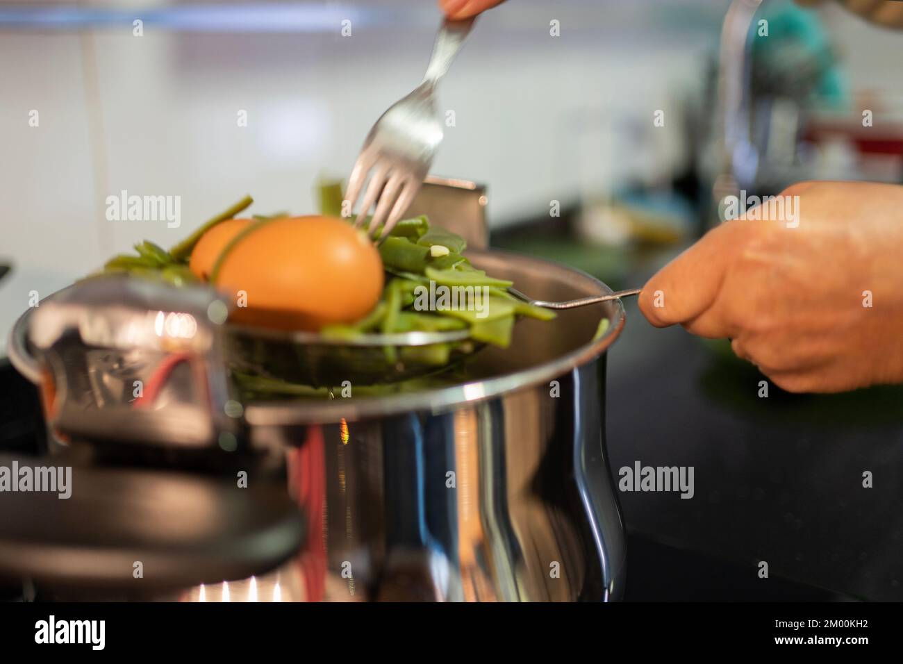 woman hands taking boiled eggs and green beens out of cooking pot with ...
