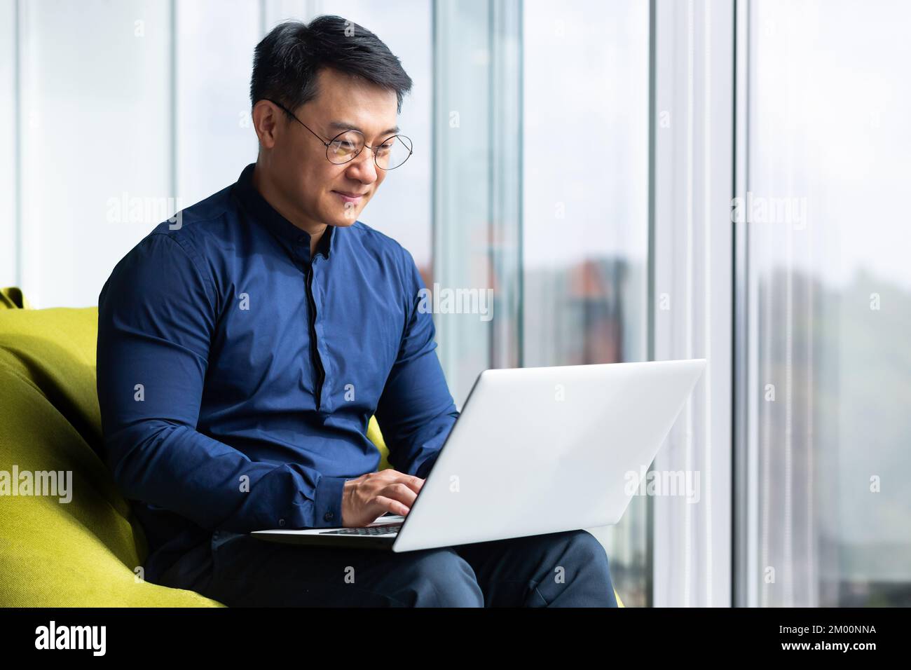 Successful and smiling asian man working with laptop inside office with ...