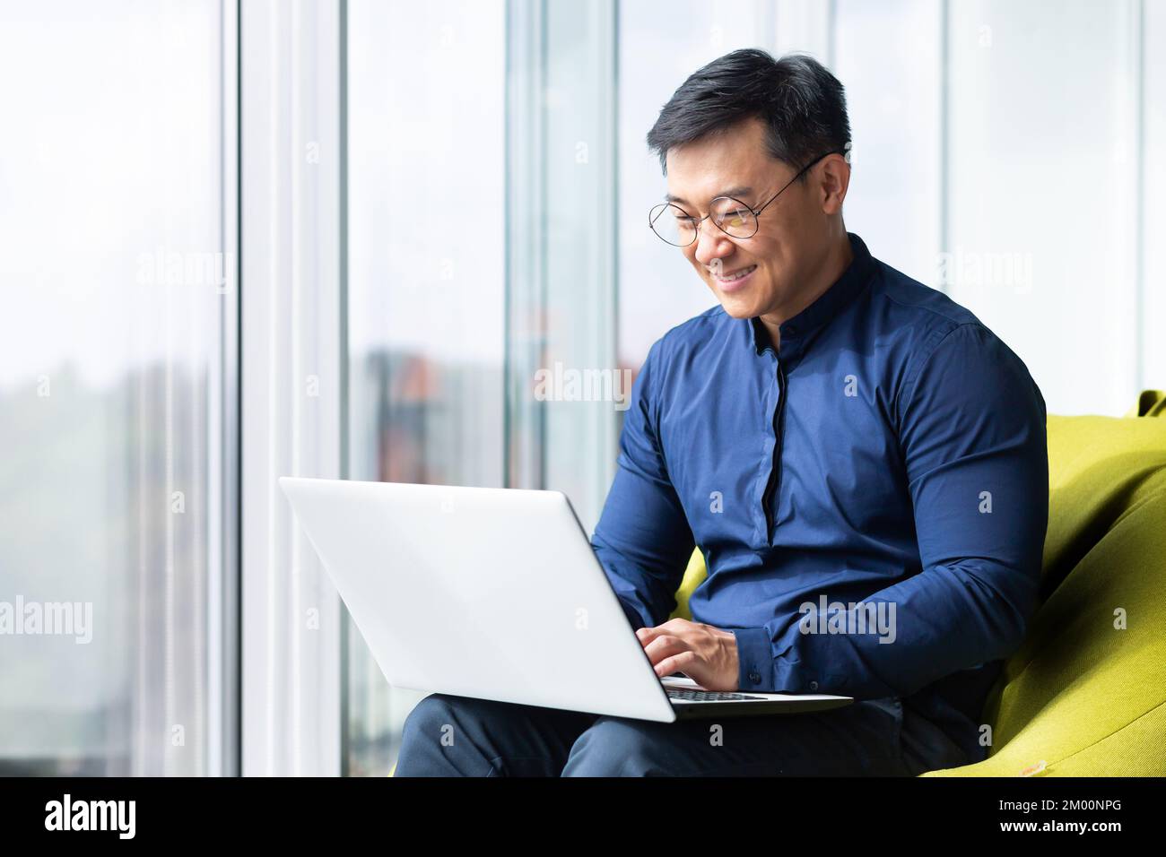 Successful and smiling asian man working with laptop inside office with ...