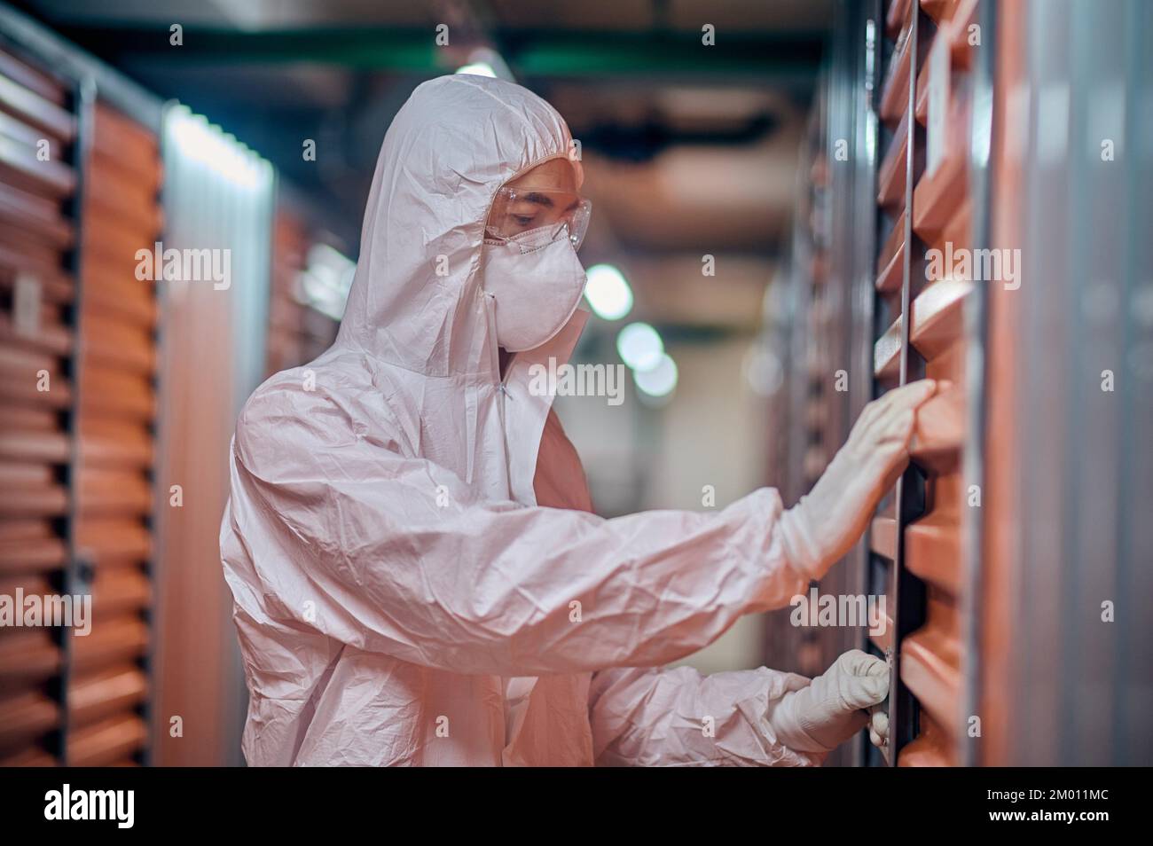 Worker in a respirator mask and hazmat suit closing the door latch of ...