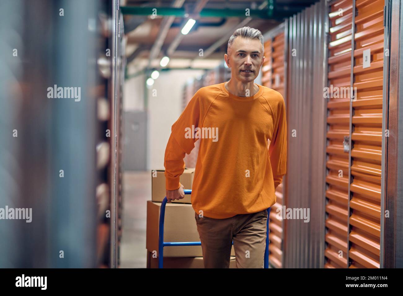 Front view of a serious male worker pulling his hand truck loaded with ...