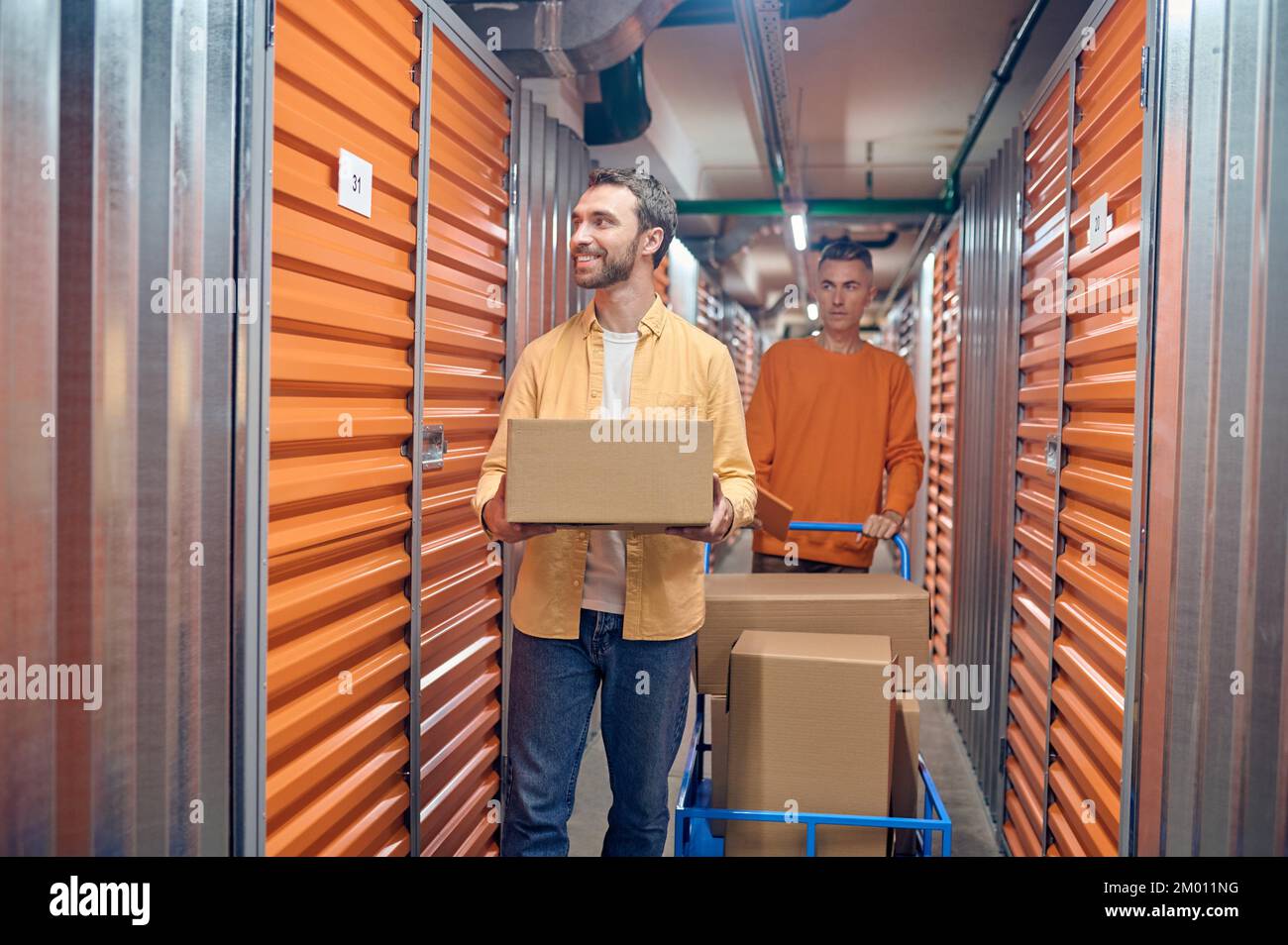 Cheerful worker with a cardboard box and his colleague with the loaded ...