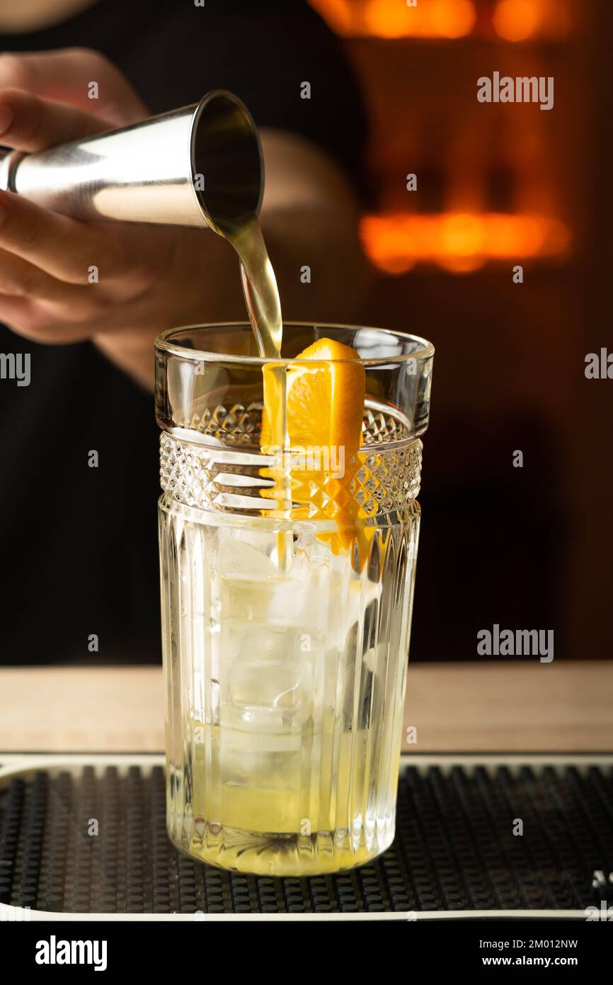 Barman pouring alcoholic drink into the glass with ice cubes on the bar counter. Copy space ...