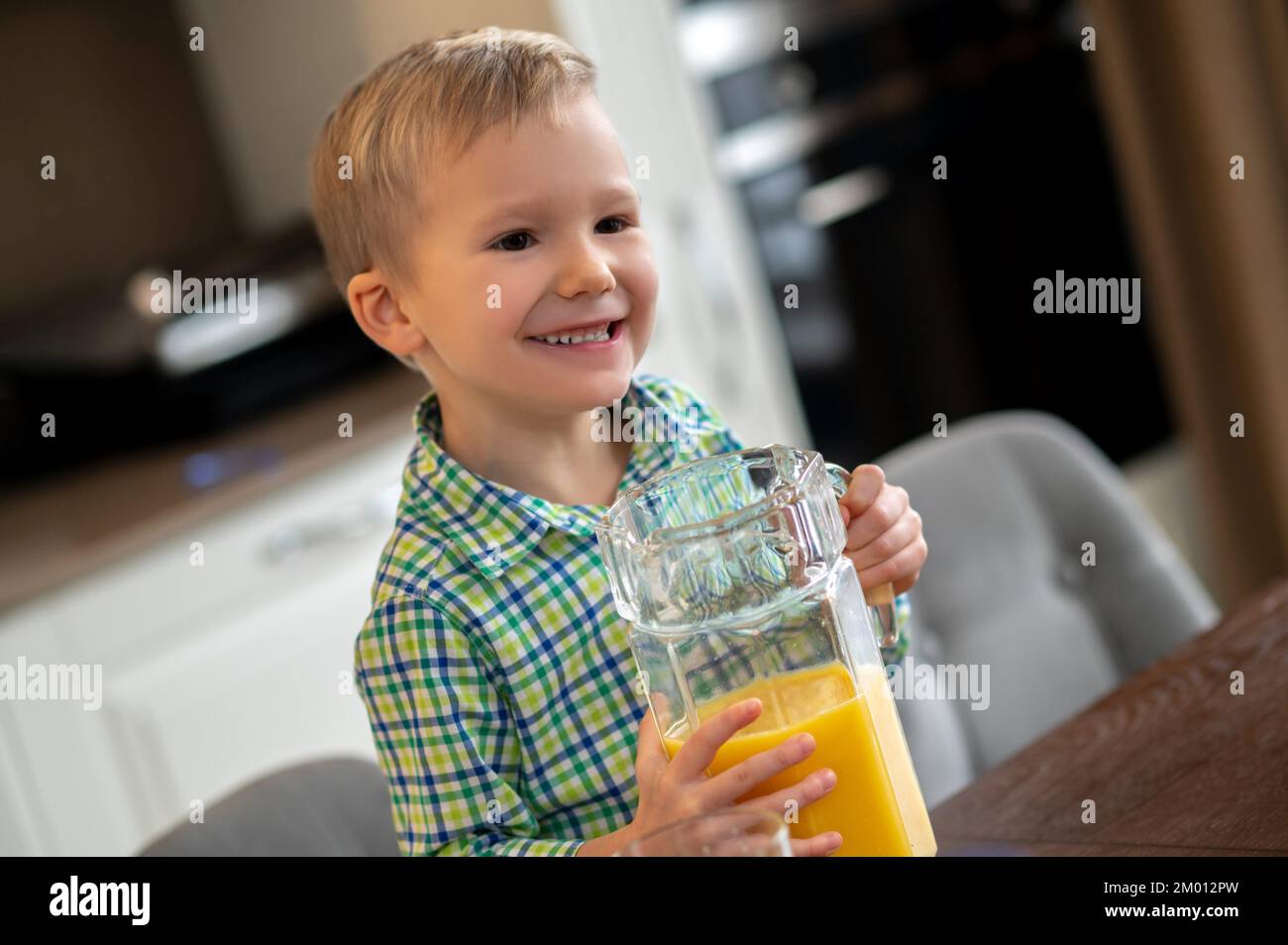 Smiling cute kid lifting the open glass pitcher filled with orange ...