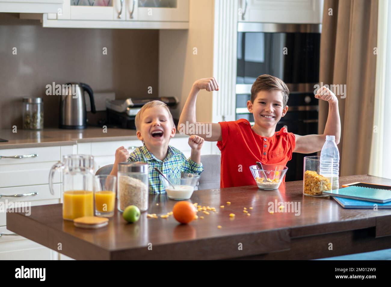 Smiling kid and his happy younger sibling flexing their muscles at the ...