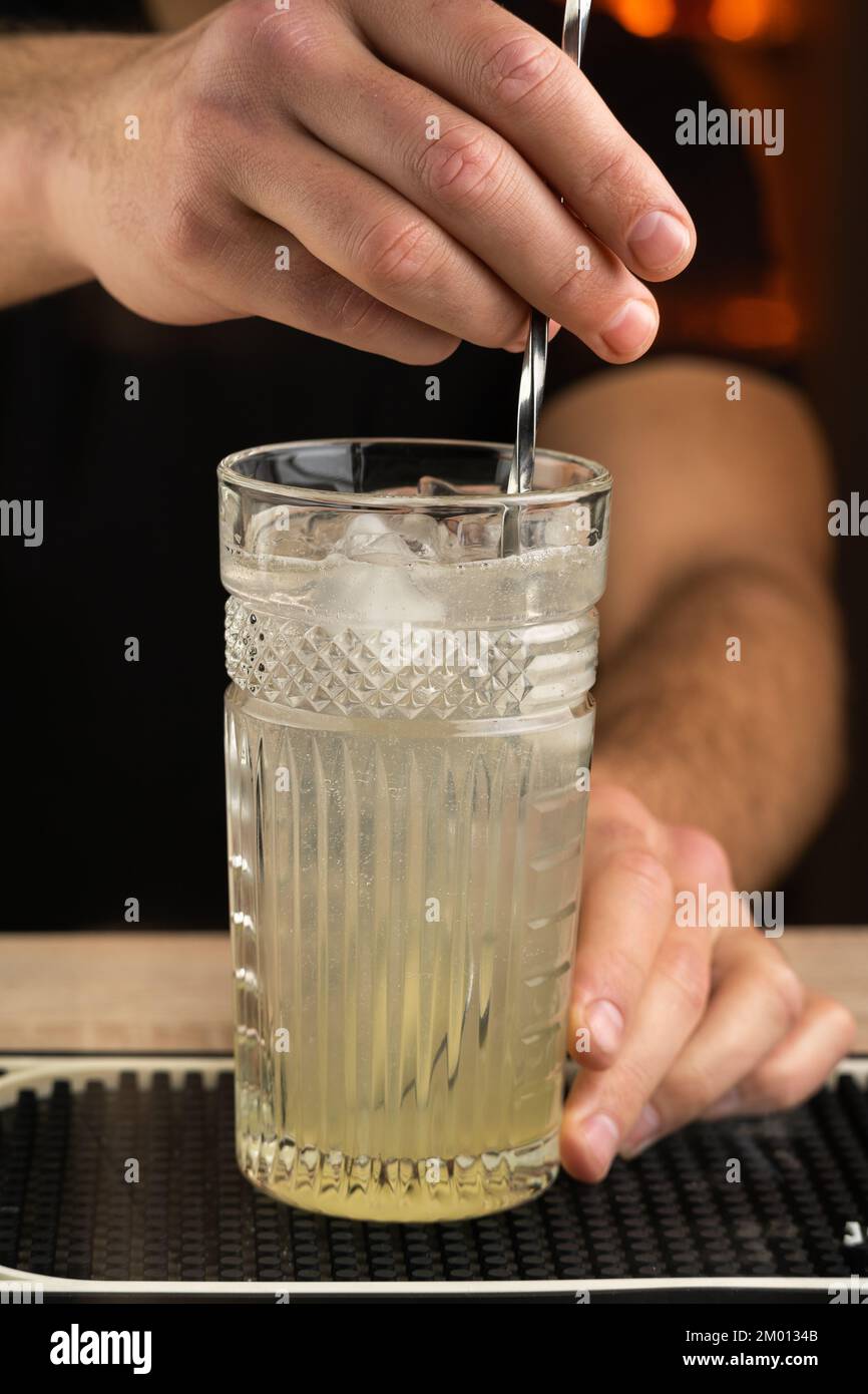Close-up of a bartender's hands stirring a cocktail with a spoon on a ...