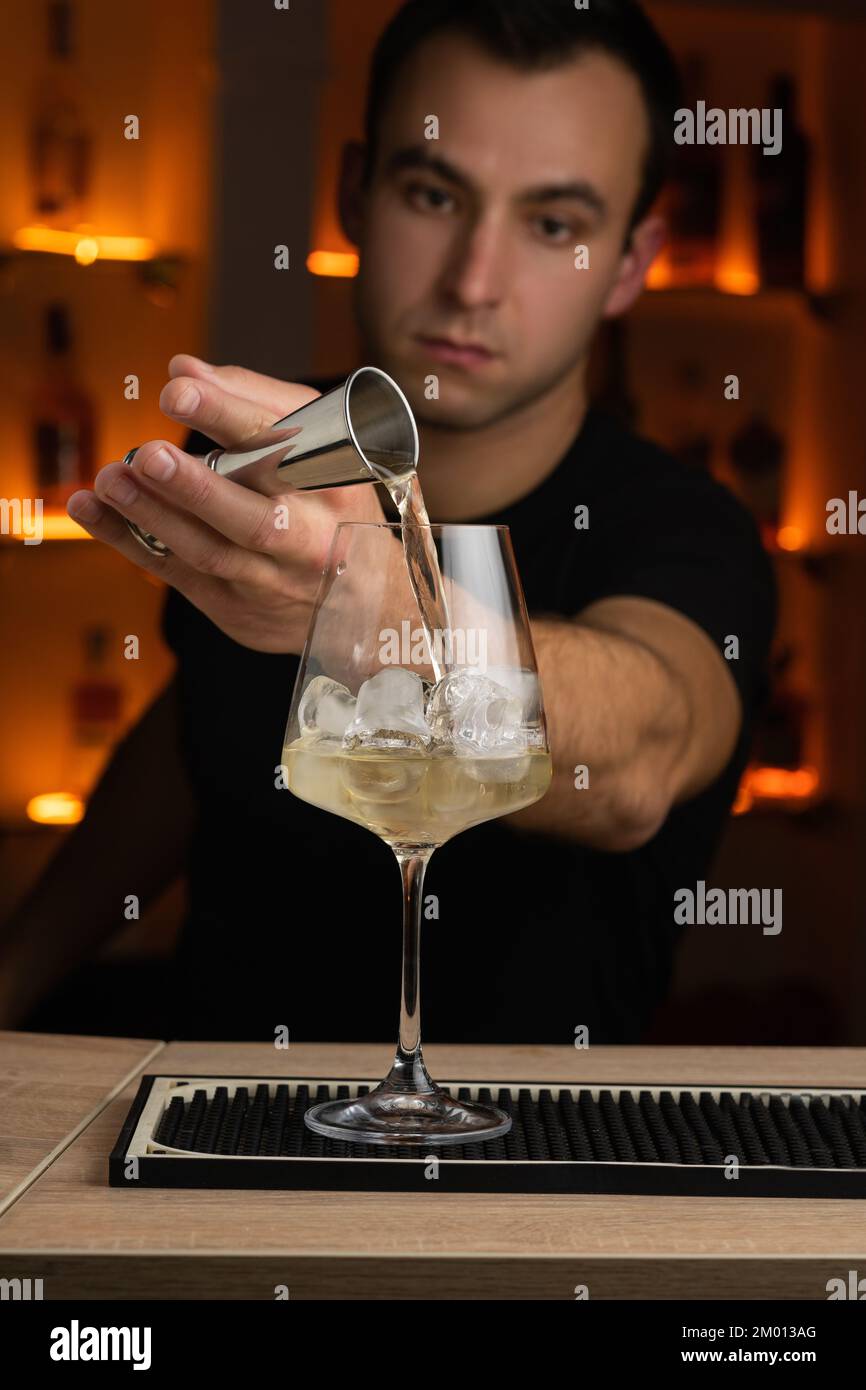 Male bartender pouring alcohol from jigger to glass with ice. Copy space Stock Photo - Alamy