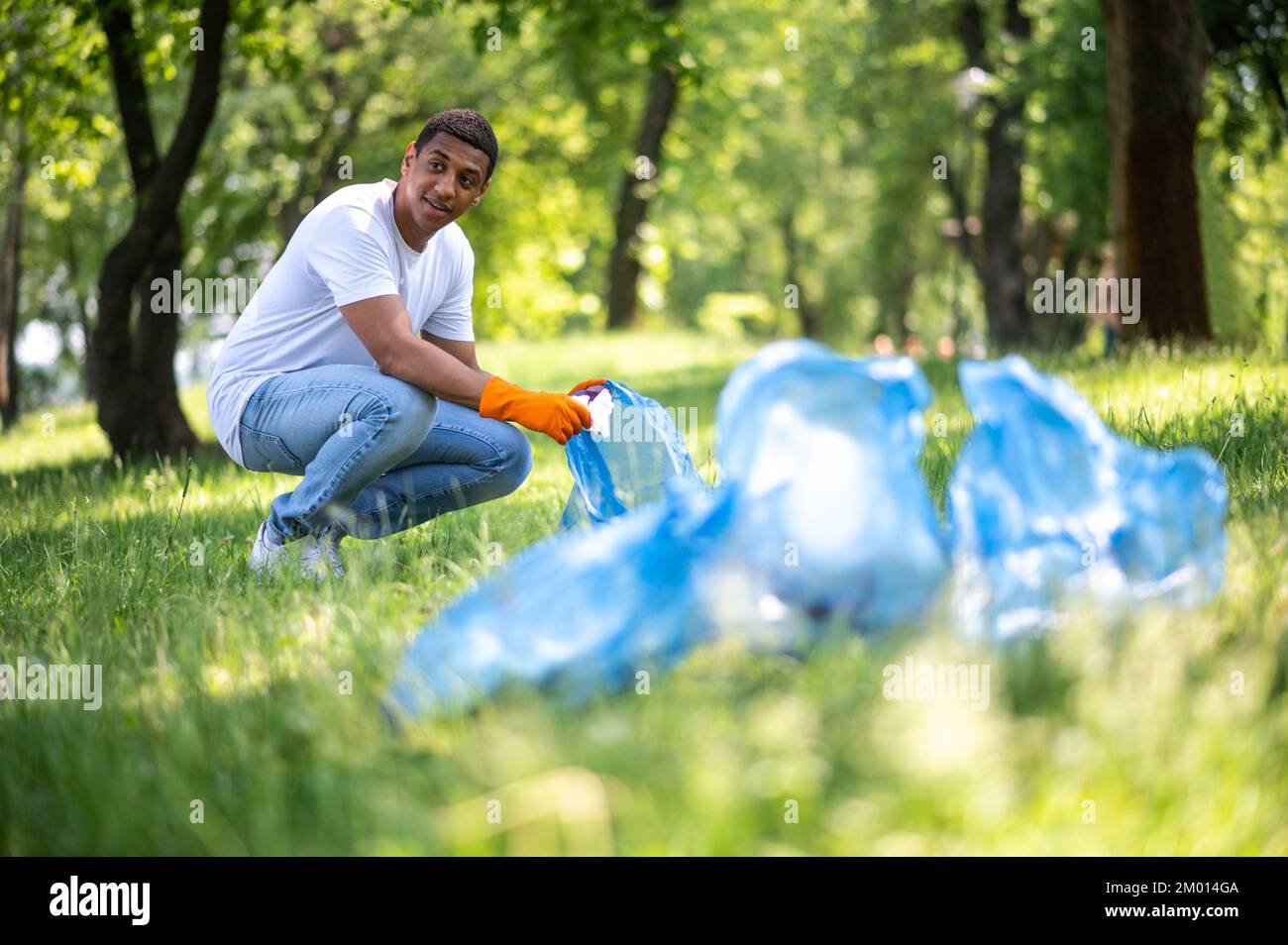 Enviroment protection. Young dark-skinned man in gloves putting garbage ...