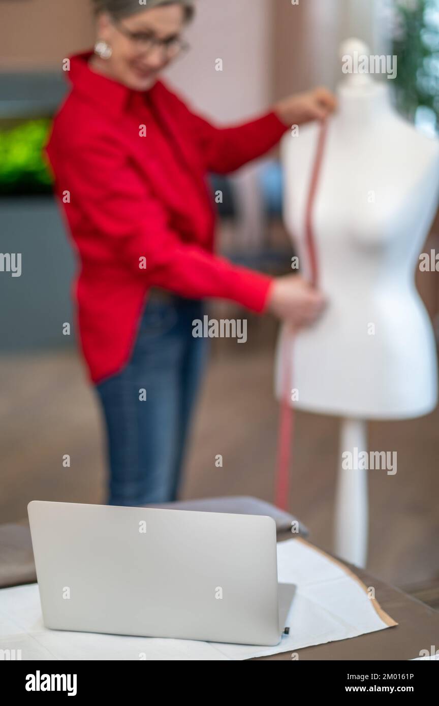 Assistant. Working laptop on table and woman standing measuring dummy ...