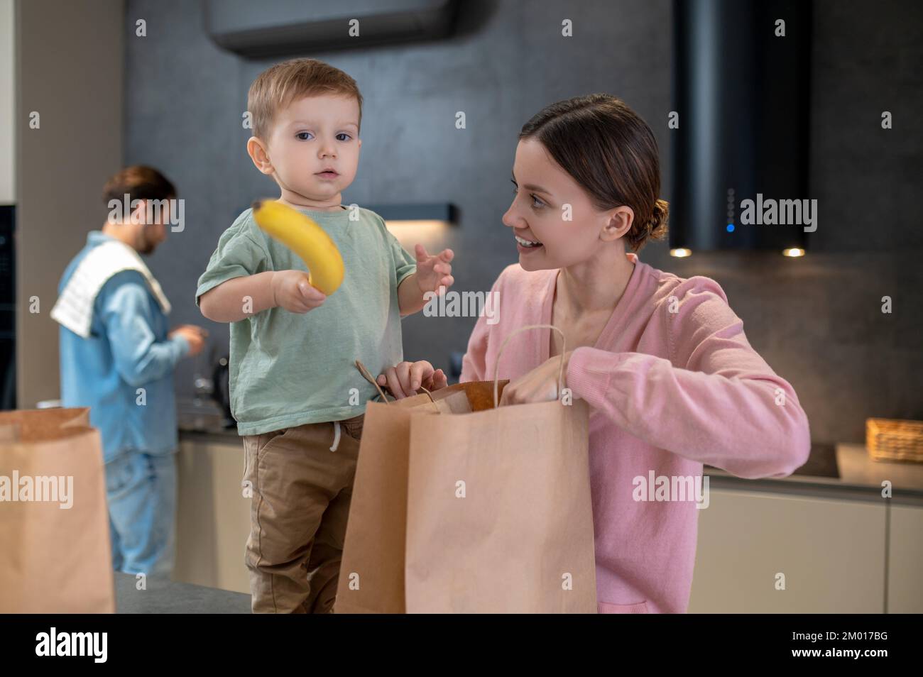 Food. Young mom with a little kid opening bags with food in the kitchen ...